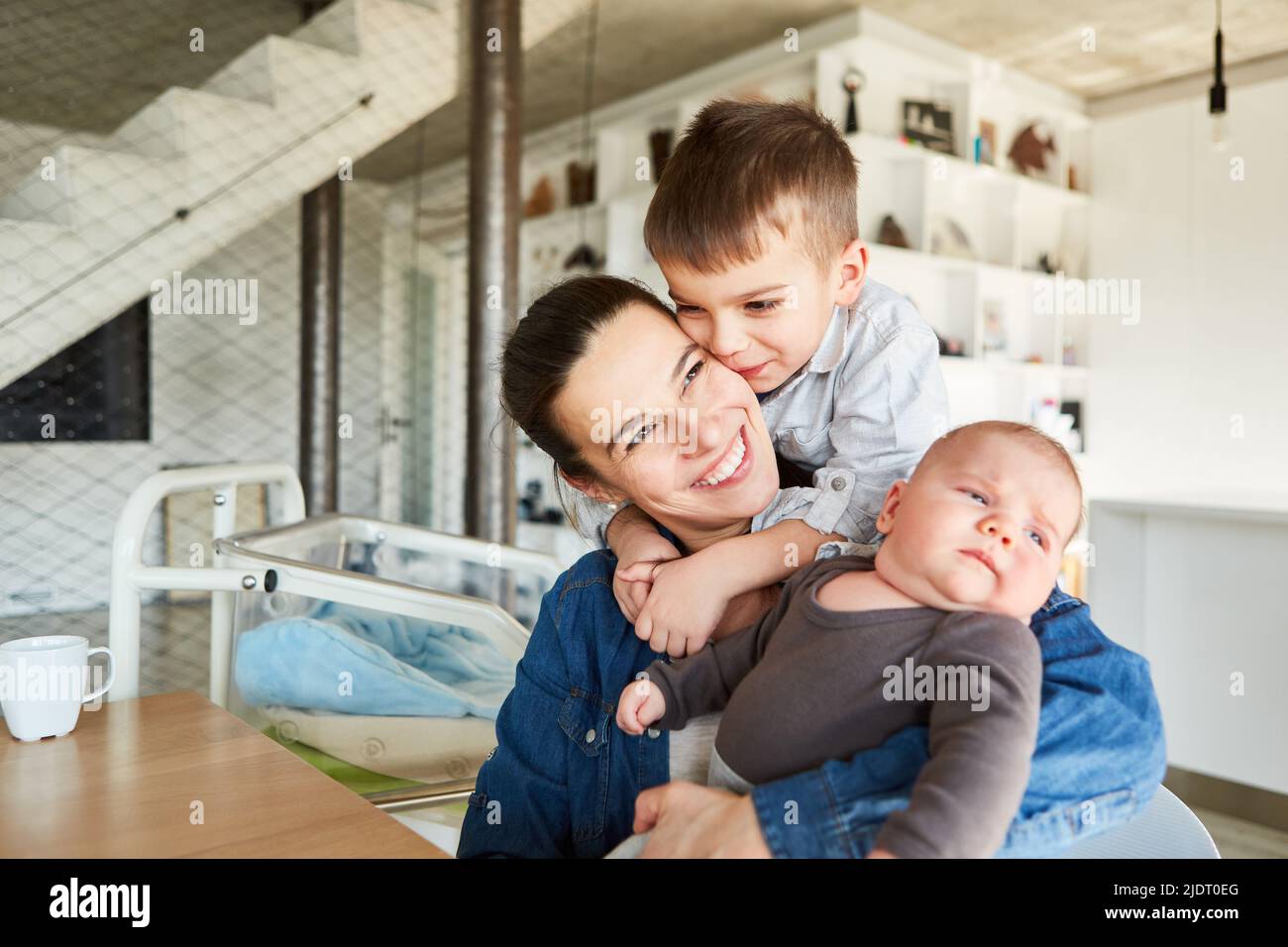 Happy single mother with baby and big brother at home in the living ...
