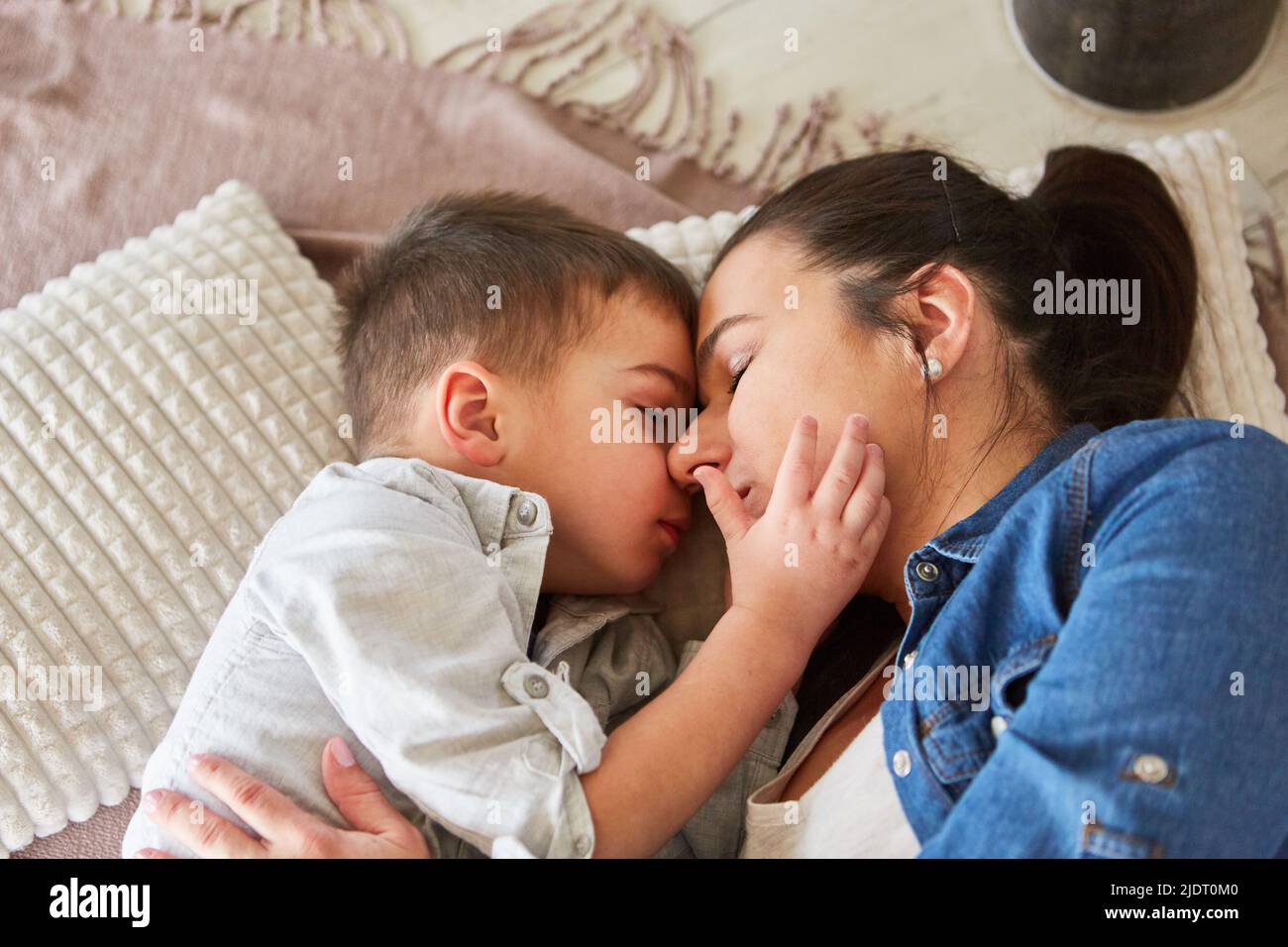 Little boy tenderly cuddling with his mother on the sofa at home in the ...