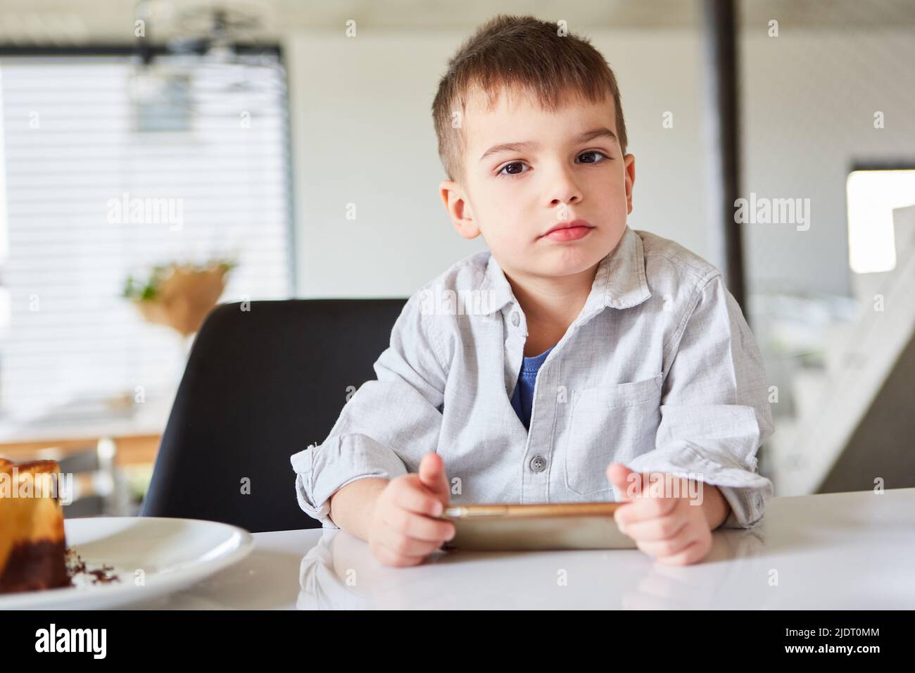 Thoughtful little boy sitting at the table in the living room with a ...