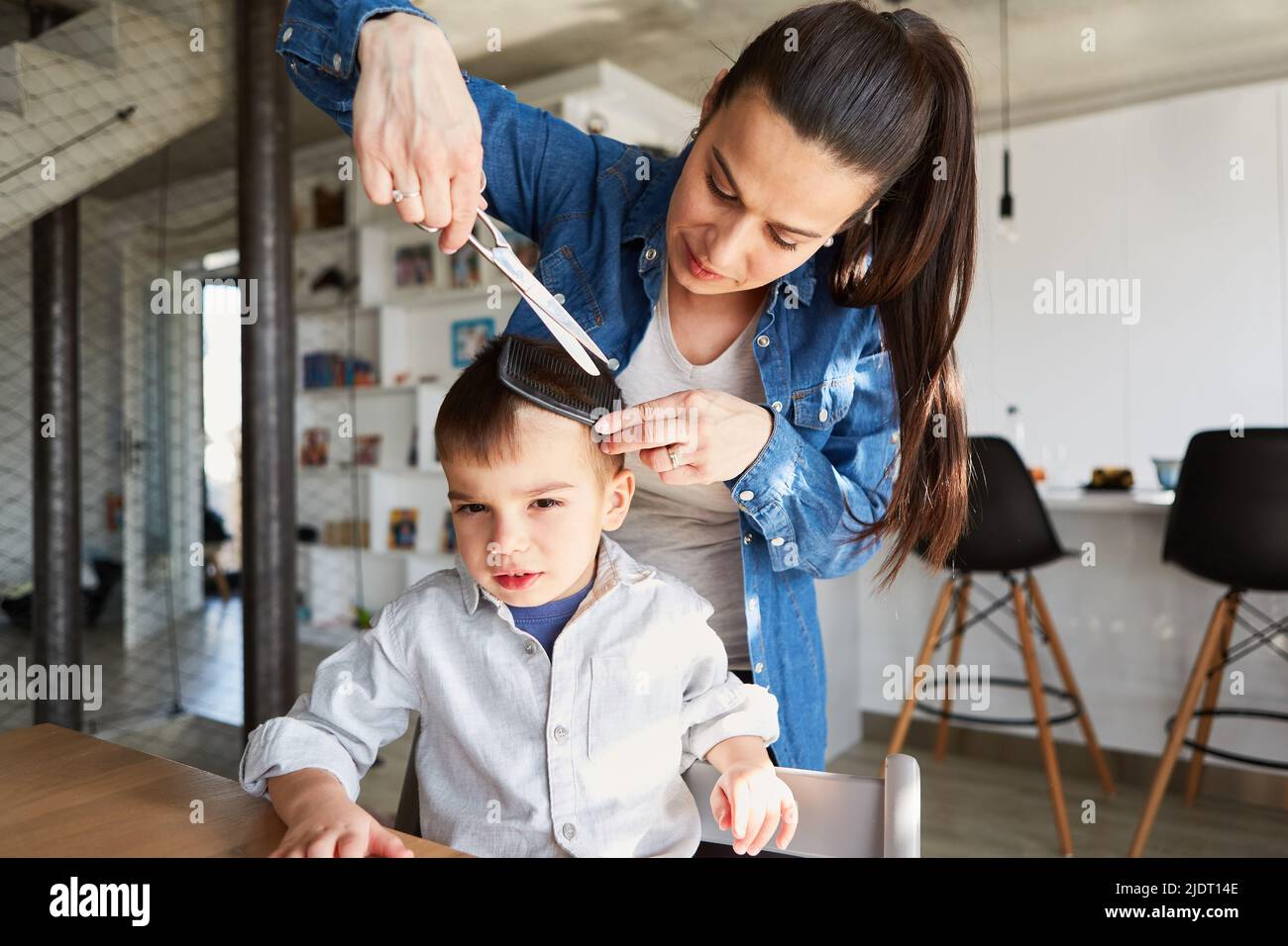 Mother or hairdresser cutting boy's hair with comb and scissors in ...