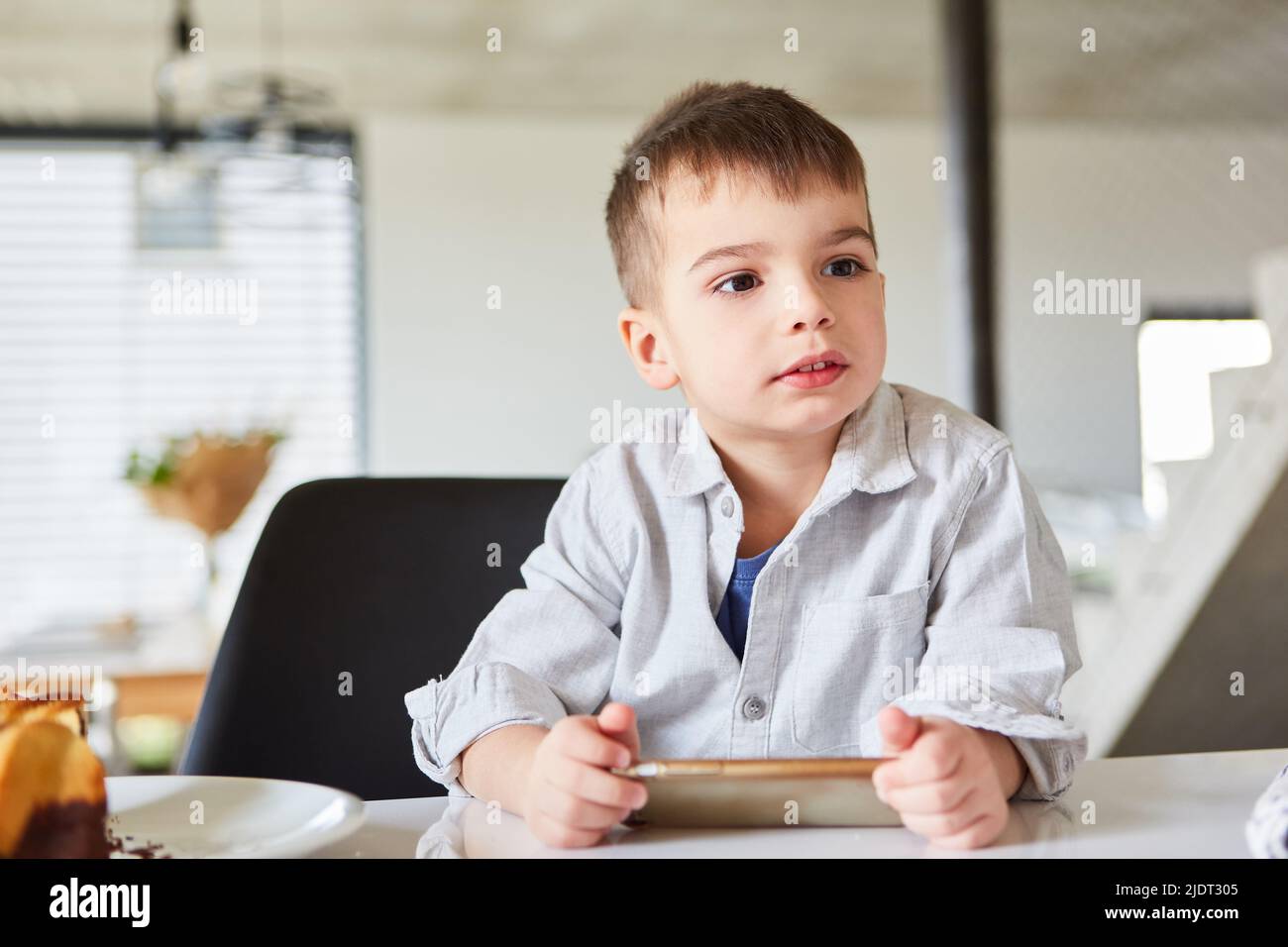 Little boy sitting alone at home at the table with a tablet computer ...