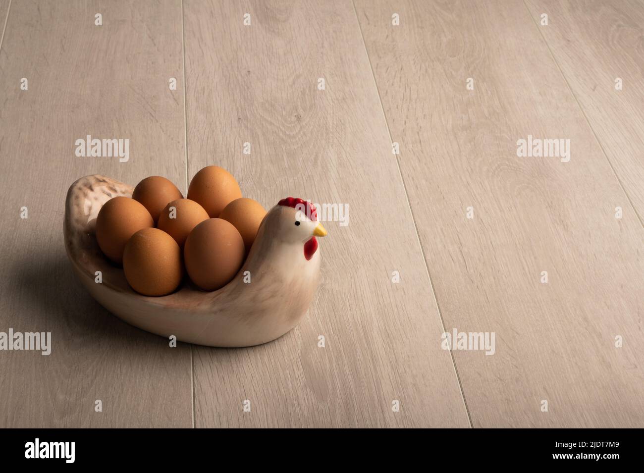 Chicken eggs in a chicken shaped dish on a light wood surface, with ...