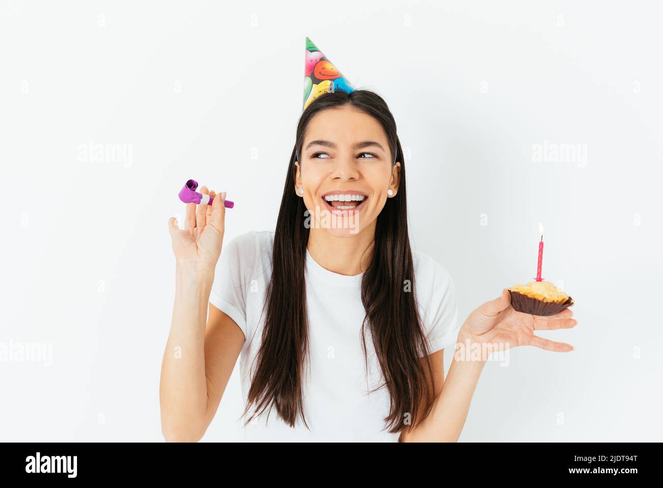 Cheerful young woman in party cap celebrating birthday holding kazoo ...