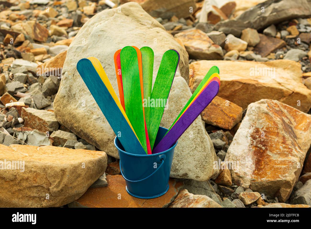Colorful wooden sticks inside of a blue bucket with stone beach ...