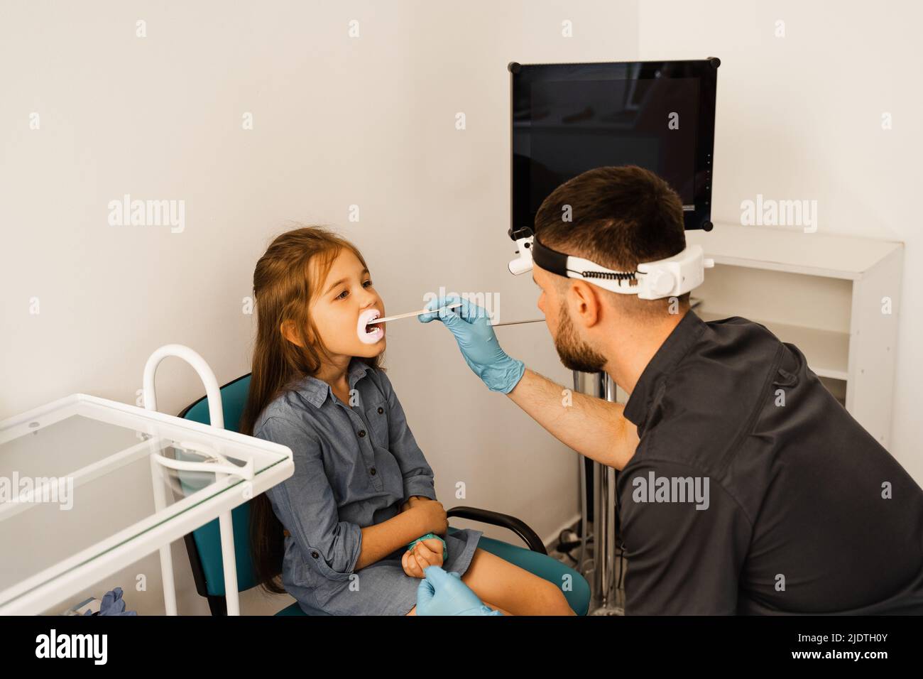 Oropharyngoscopy procedure. Otolaryngologist examines child throat with ...