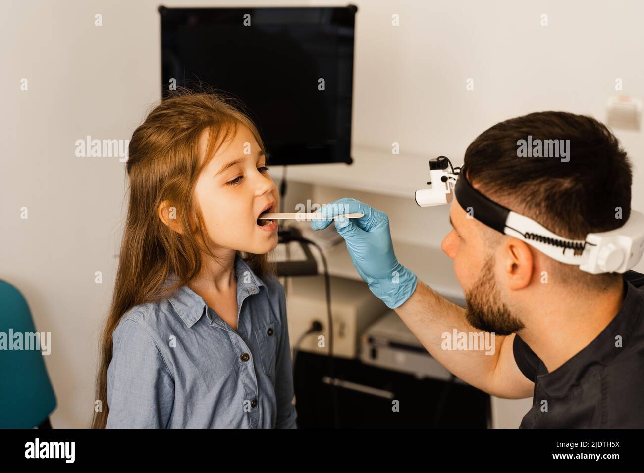Oropharyngoscopy procedure. Otolaryngologist examines child throat with ...