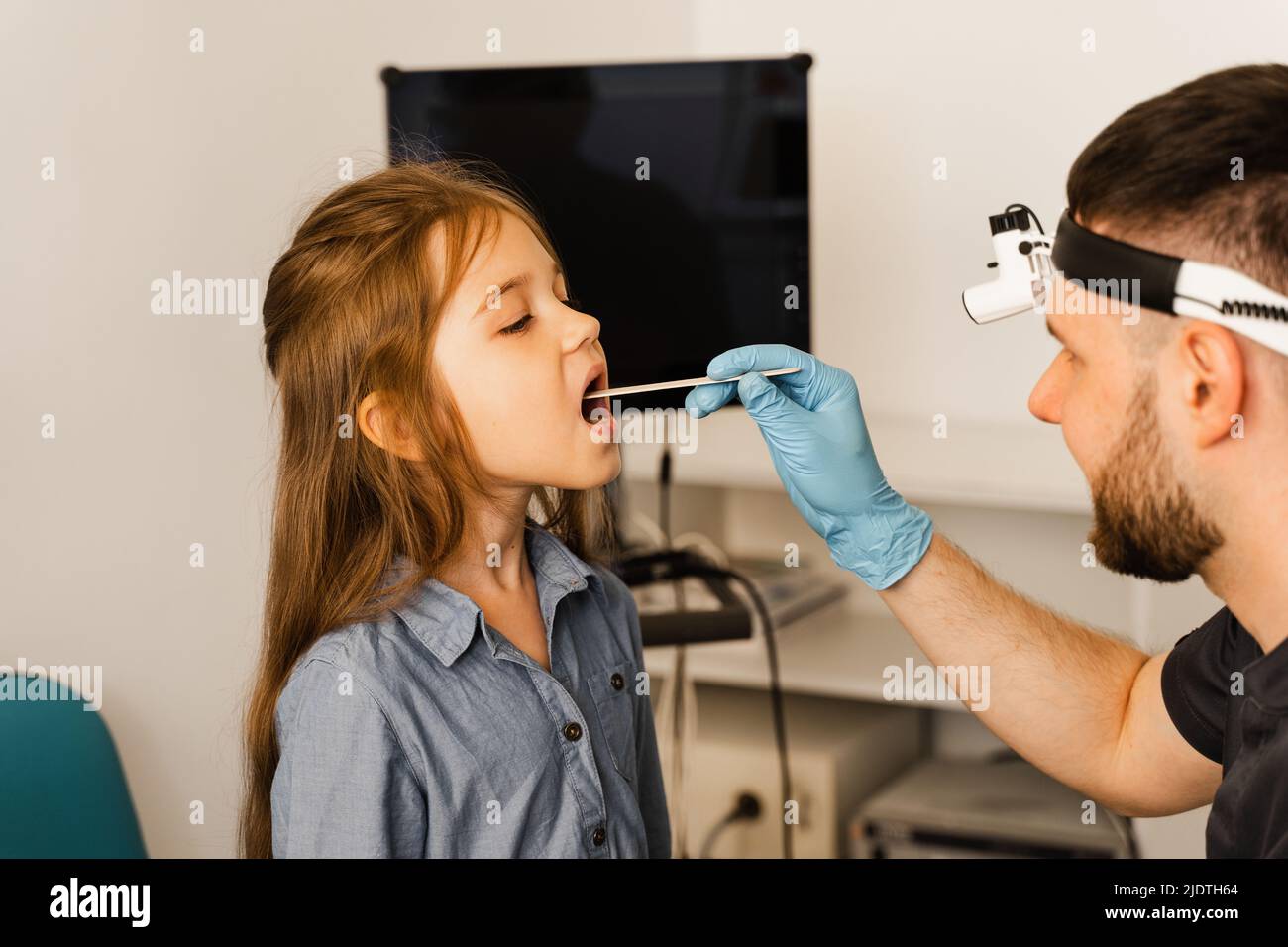 Oropharyngoscopy procedure. Otolaryngologist examines child throat with ...