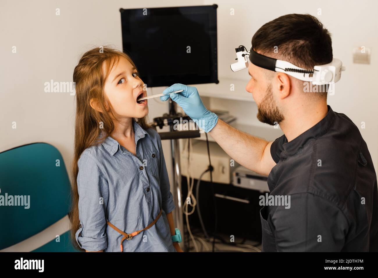 Oropharyngoscopy procedure. Otolaryngologist examines child throat with ...