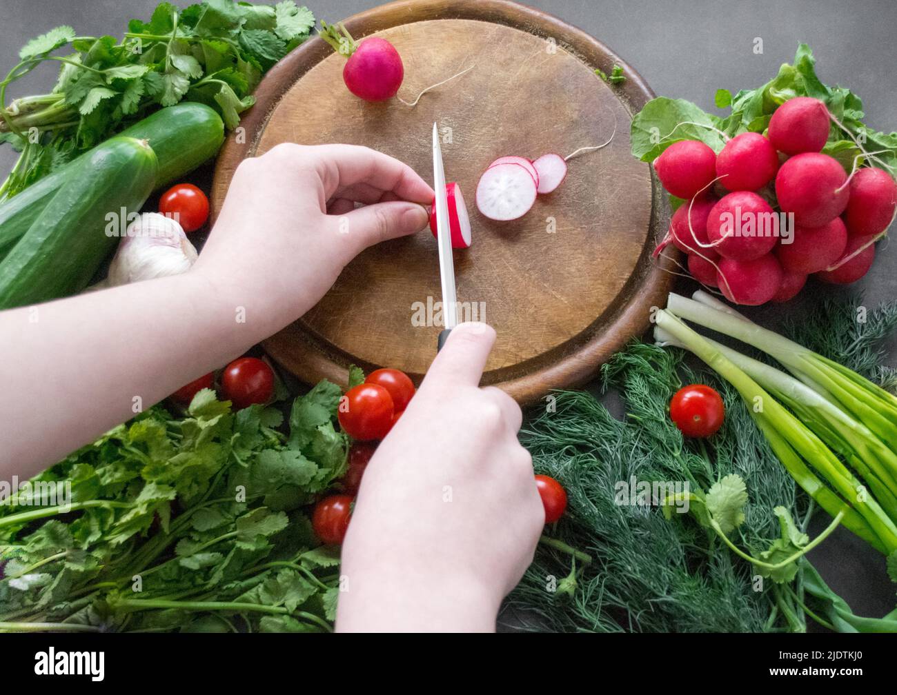 Hands cutting radishes with a white ceramic knife on a round wooden ...