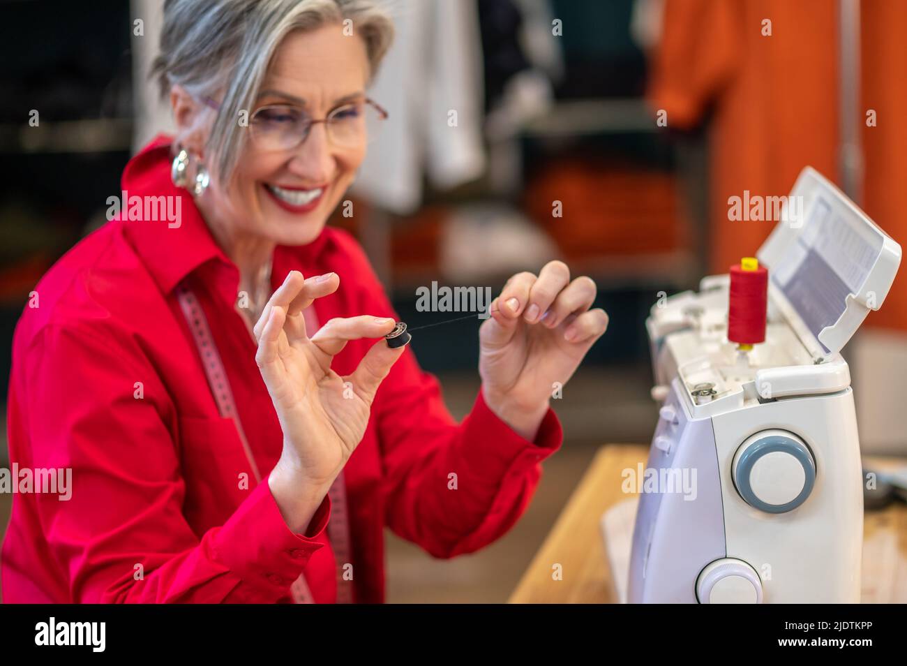Smiling woman showing sewing spool of thread Stock Photo - Alamy