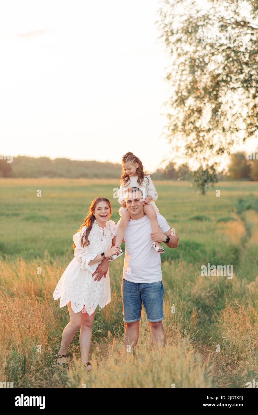 Happy family walks on meadow and father carries daughter on his shoulders during outing Stock ...