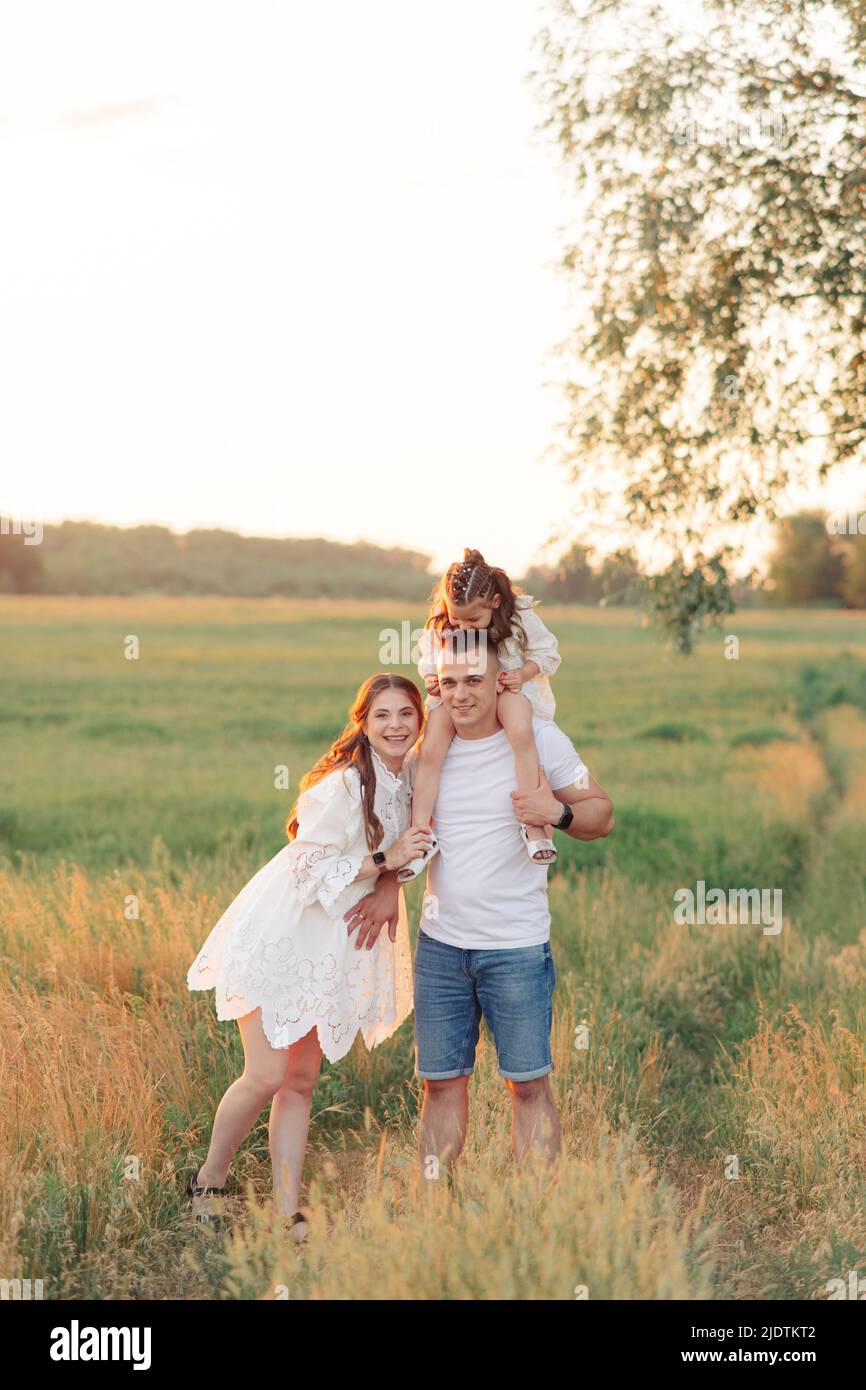 Happy family walks on meadow and father carries daughter on his shoulders during outing Stock ...