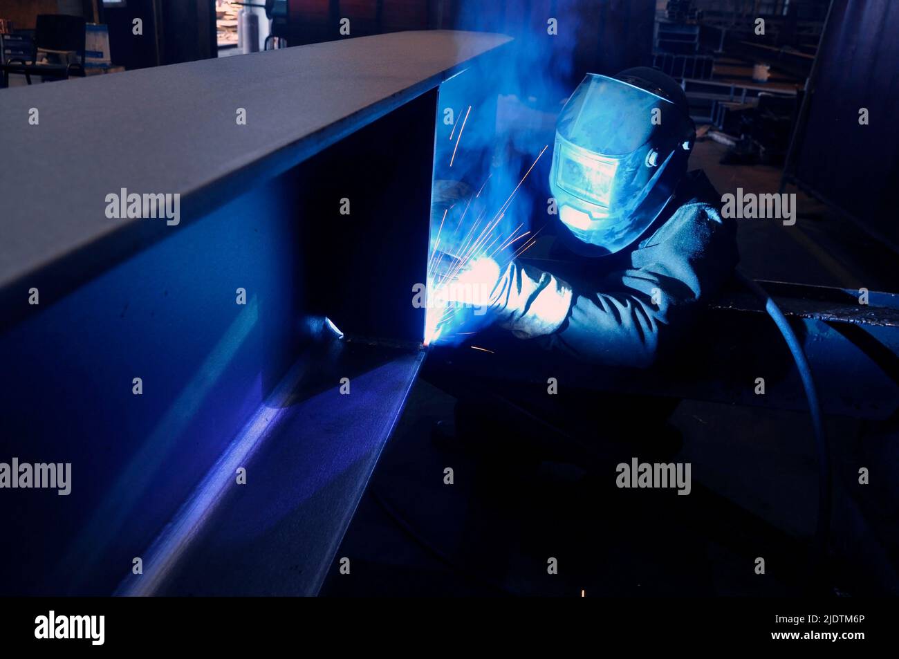 A welder in protective overalls and a welding mask welds metal ...