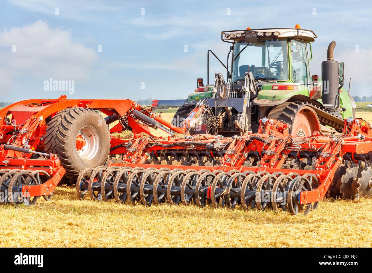A red disc harrow clings to a wheeled agricultural tractor for ...
