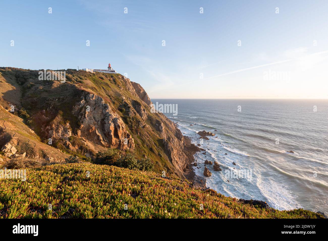 Cabo da Roca lighthouse by coastal rocks and cliffs covered in green ...