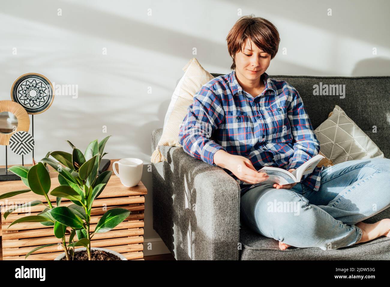 Woman sit on the sofa couch and relax while reading a book at home in ...