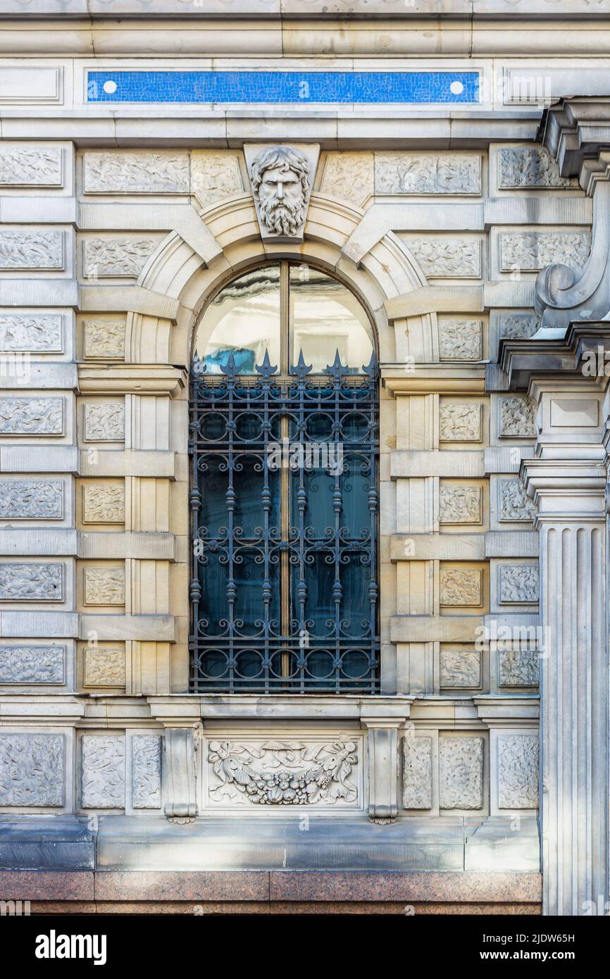 Arched window with a bas-relief and a figured iron grate against a gray ...