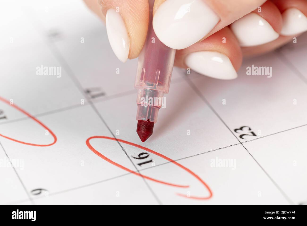 female hand marking with a red pen on a calendar circles the day ...