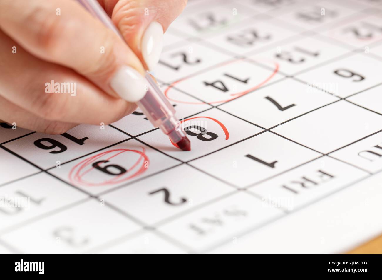 female hand marking with a red pen on a calendar circles the day ...