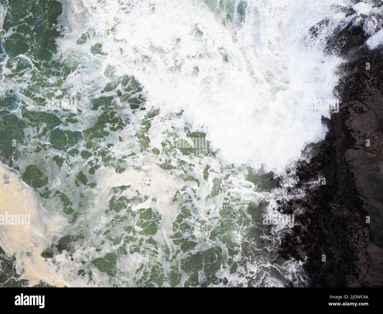 Top view of the raging ocean. White foamy waves crash against the shore ...