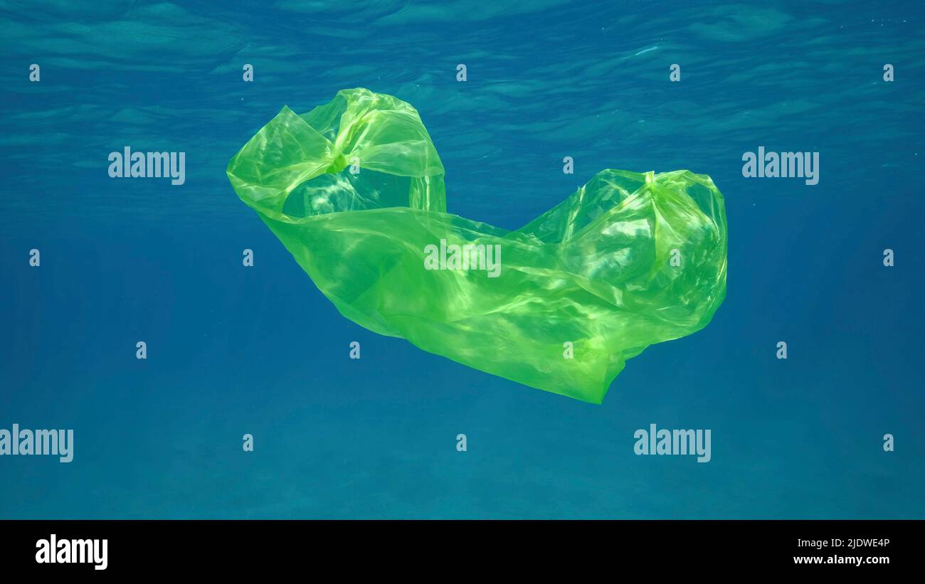 Plastic pollution, Yellow plastic bag swims underwater reflecting on ...