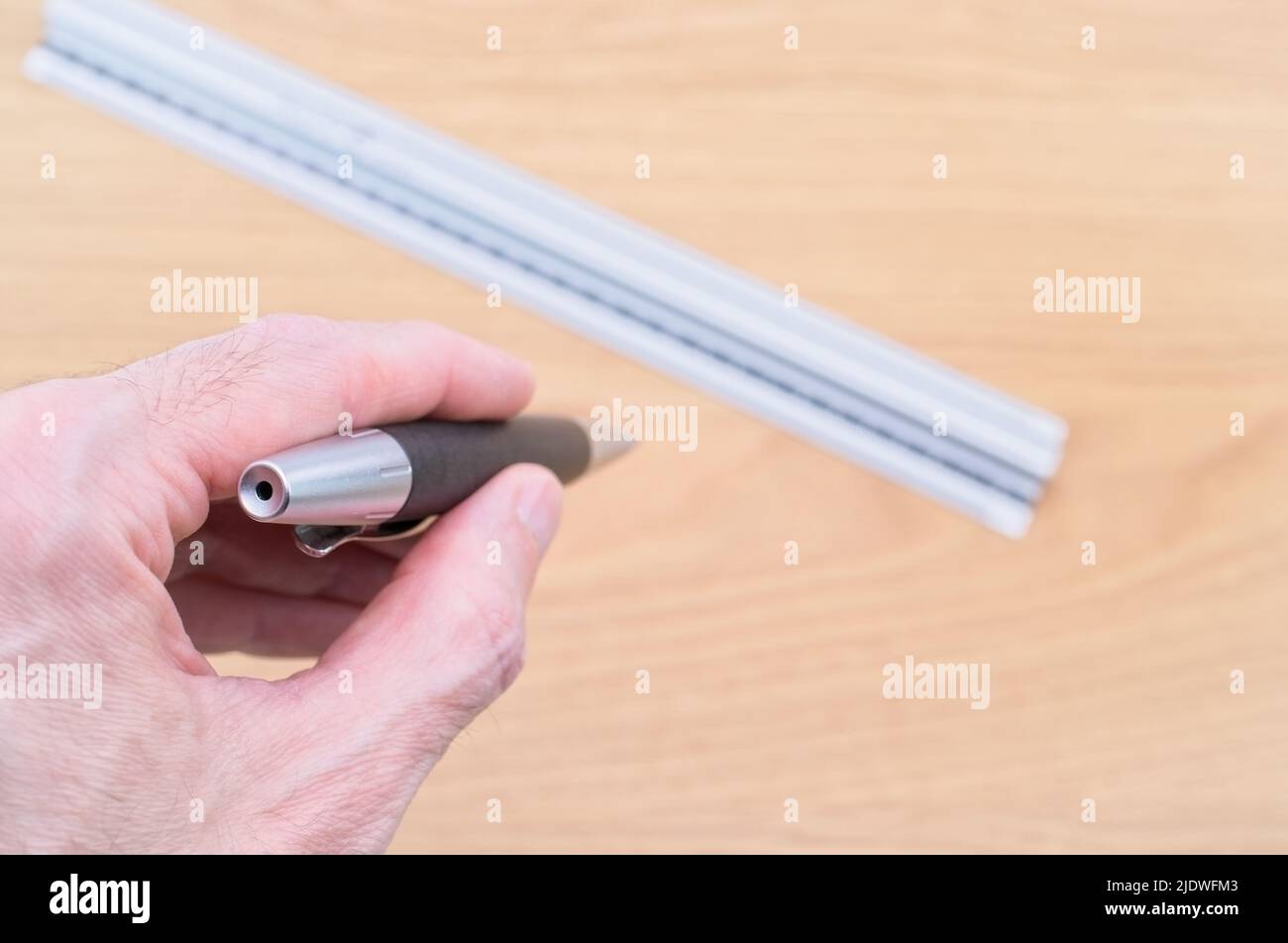 metal decimal ruler with hand holding pencil on a wooden desk ...