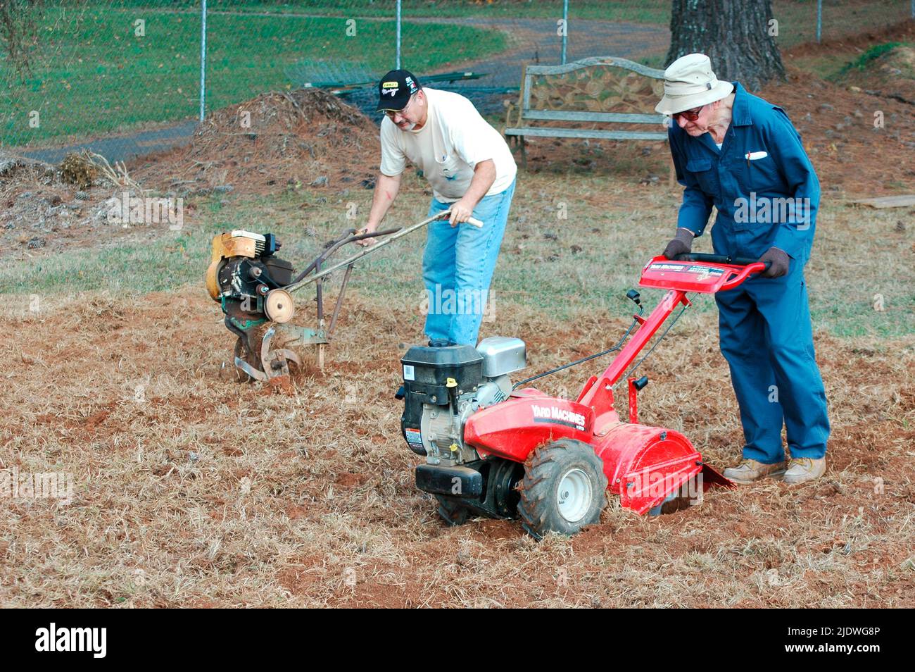 Men roto tilling a public lawn to put in garden with tillers, front and ...