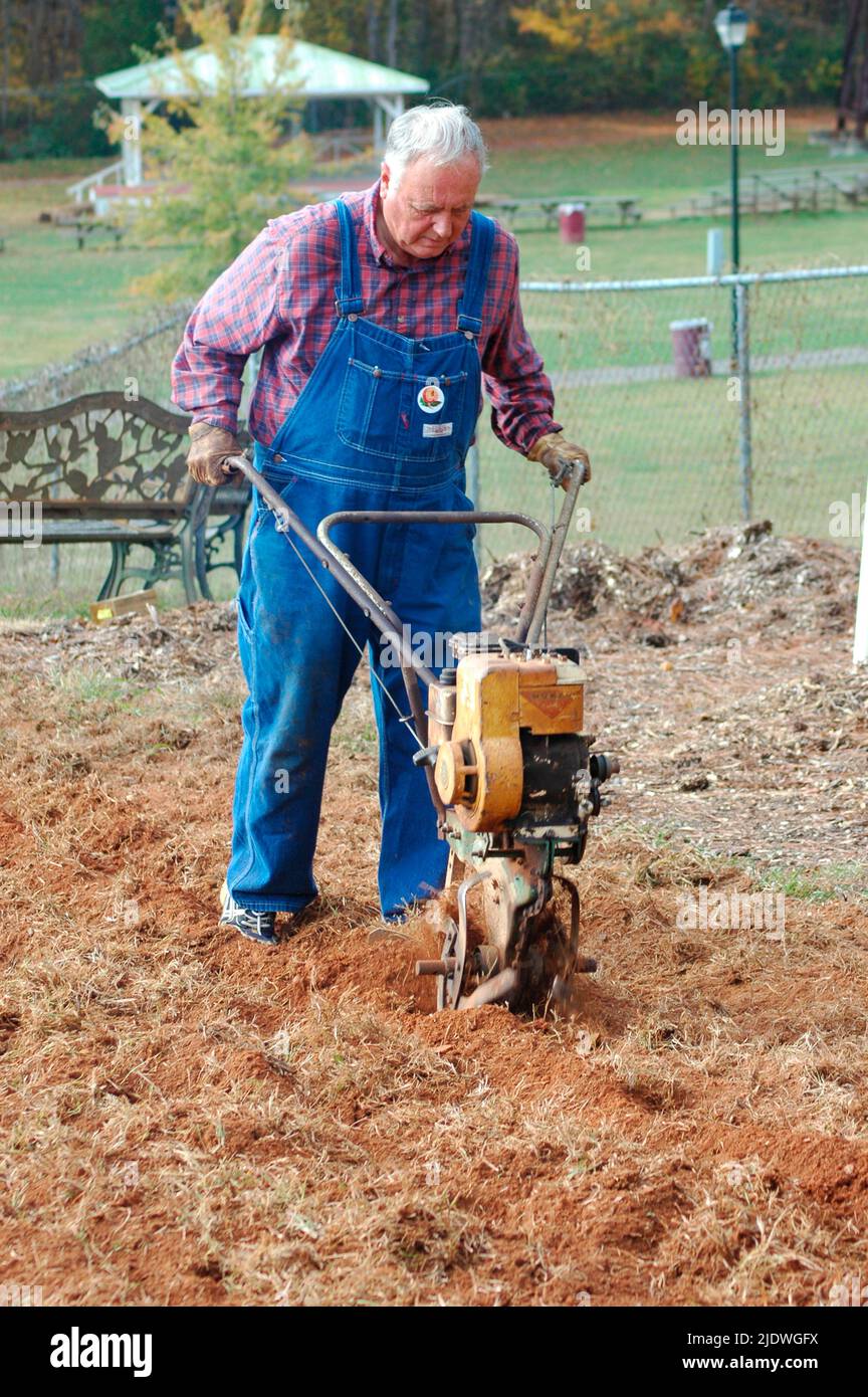 Men roto tilling a public lawn to put in garden with tillers, front and ...