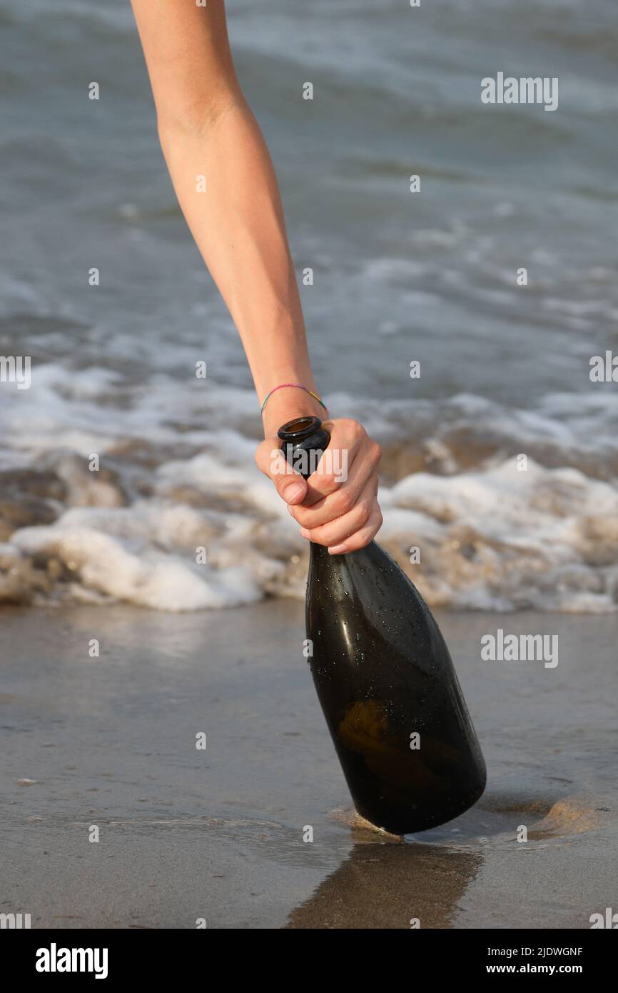 hand picking up a glass bottle on the seashore and perhaps it contains ...