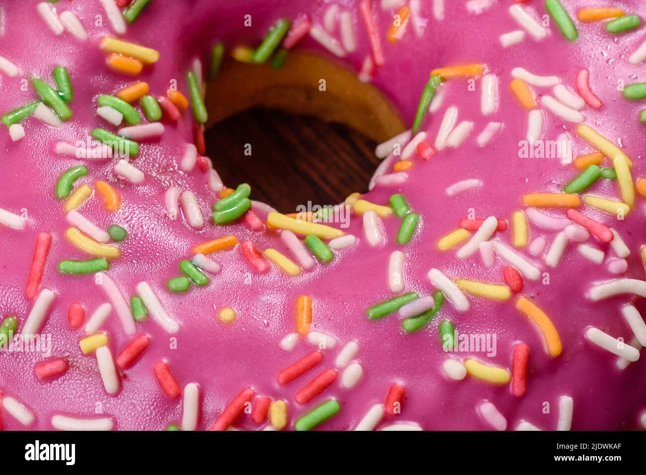 A beautiful doughnut with pink glaze and colored sprinkle on a dark ...