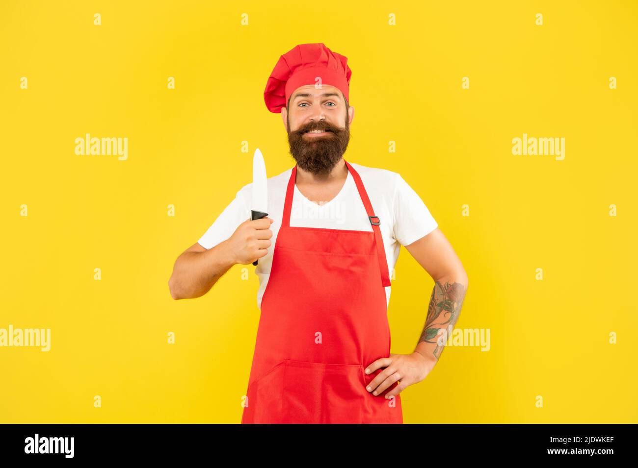 Happy man in red apron and toque holding cooks knife yellow background ...