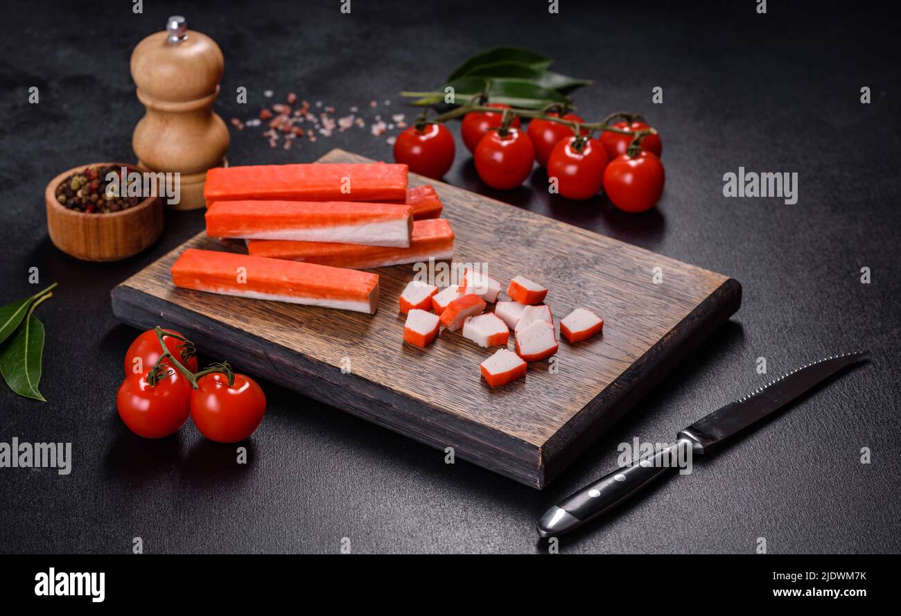 Sliced crab sticks on a cutting Board with a knife. On black rustic ...