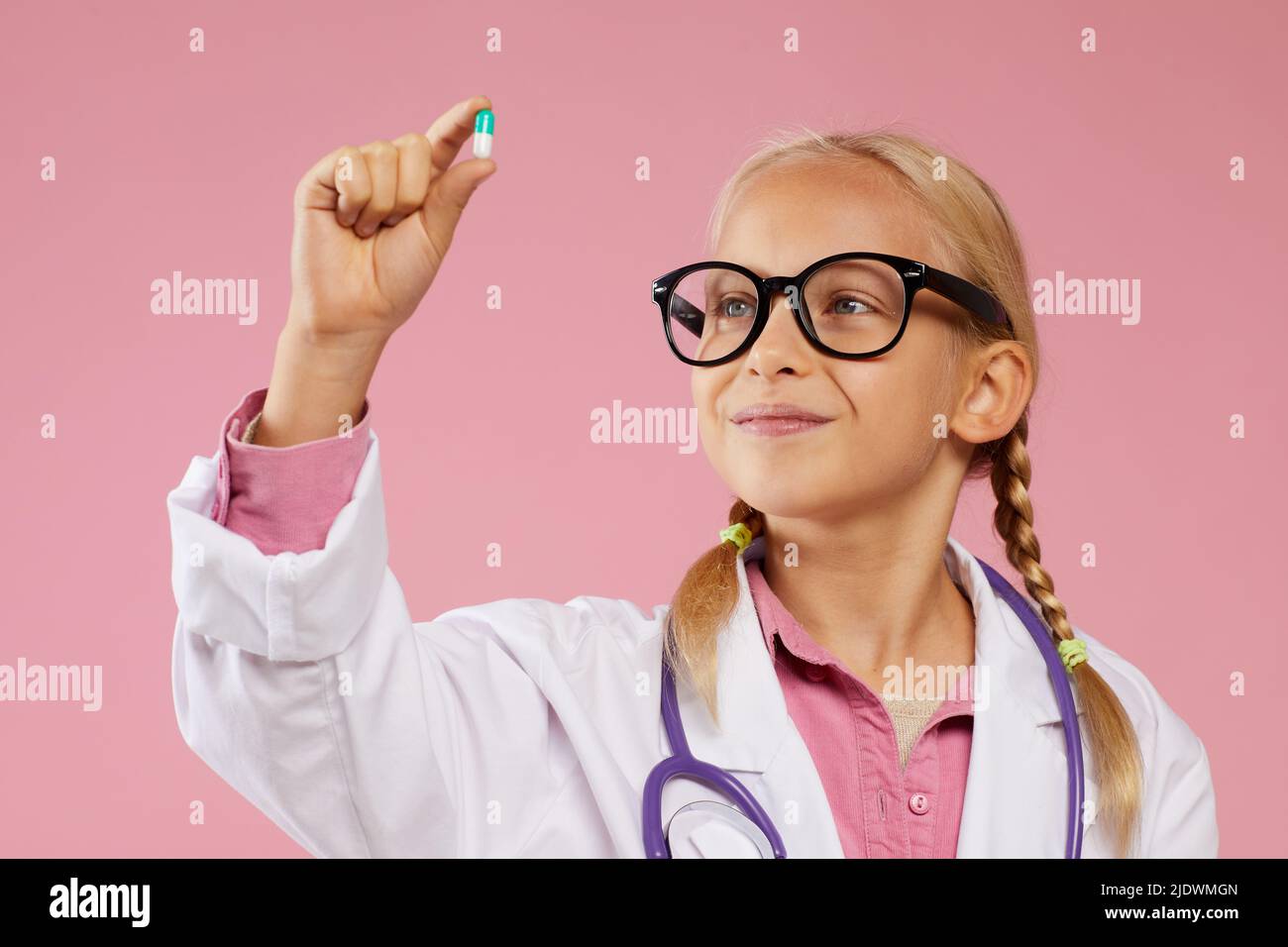 Content clever pretty girl in doctors dress standing against pink ...
