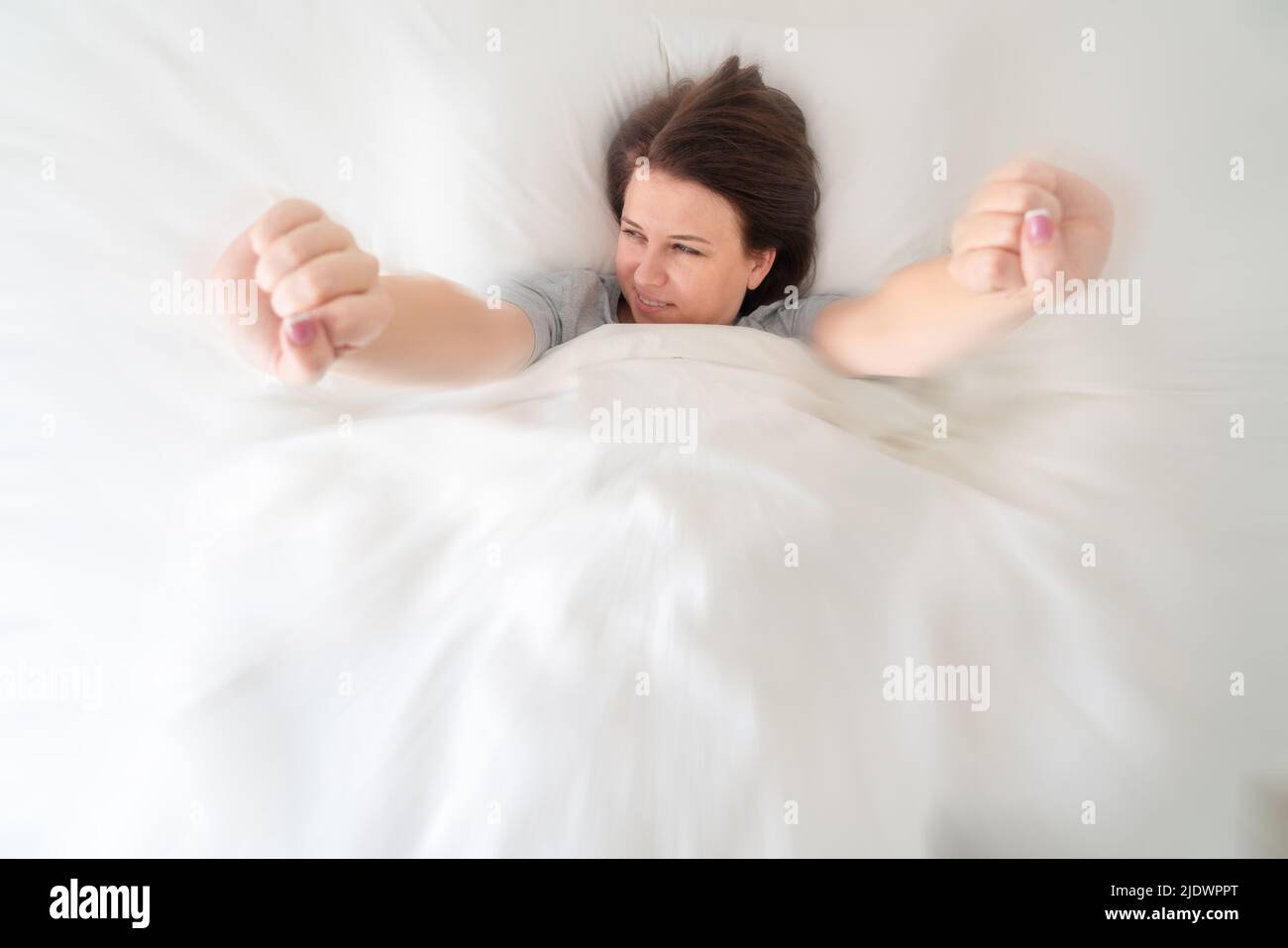 Portrait of young beautiful woman in bed stretching in the morning with ...