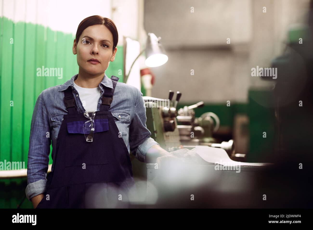 Portrait of content skilled gritty woman in workwear standing at ...