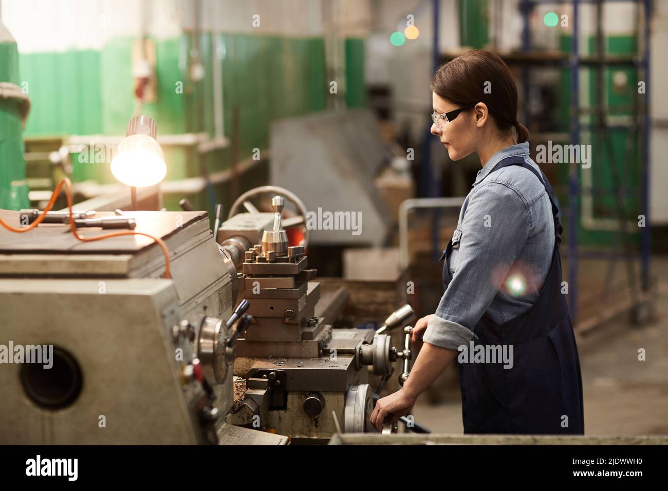 Concentrated middle-aged female industrial laborer in overalls susing ...