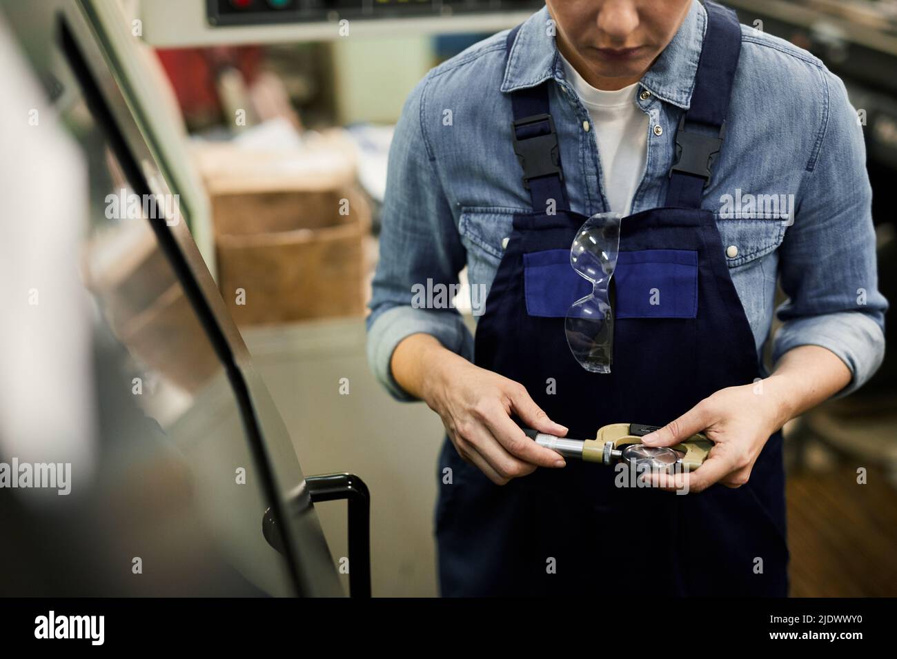 Close-up of serious female factory worker with safety goggles hanging ...
