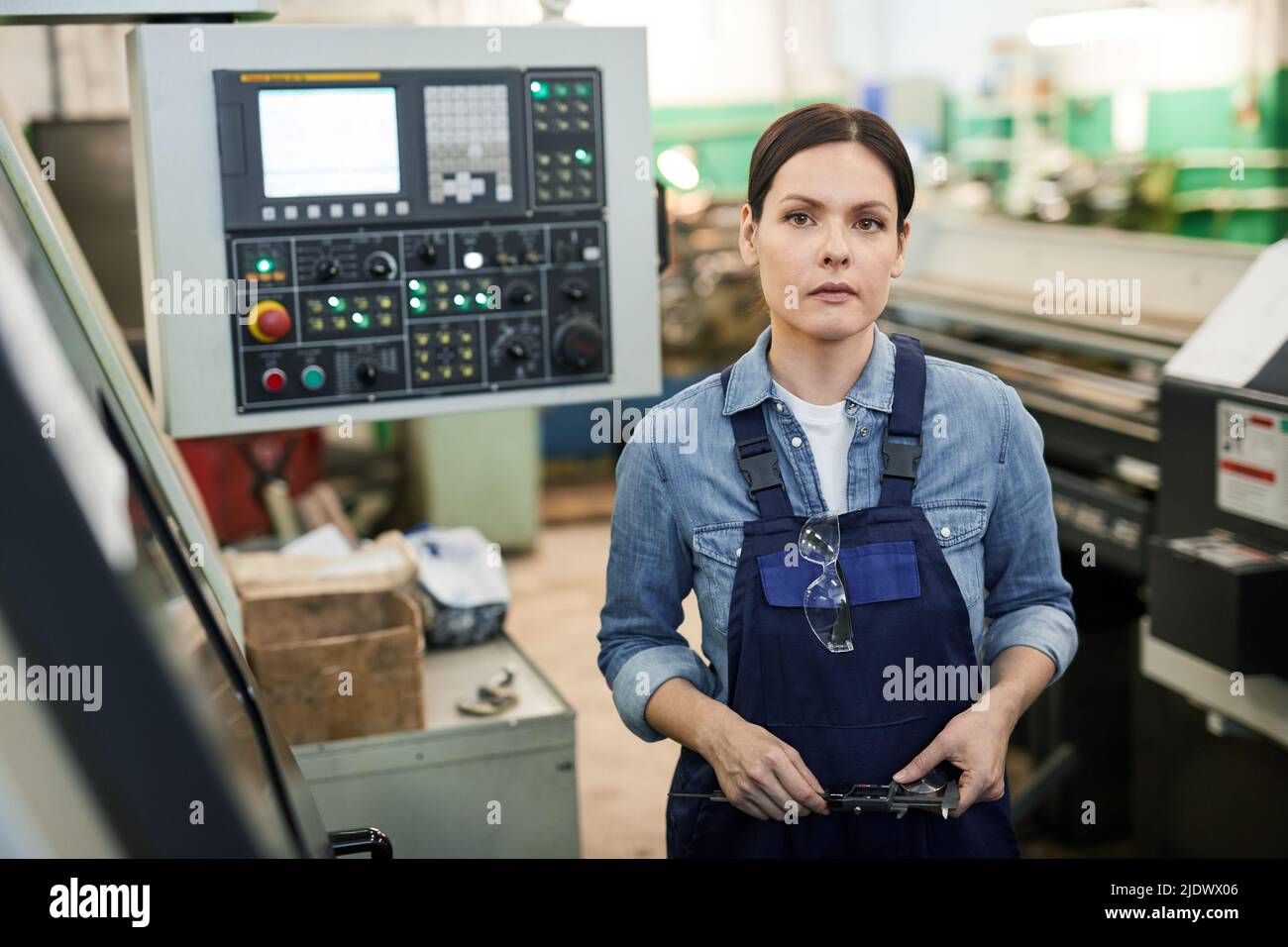 Portrait of serious attractive female factory worker in overalls ...