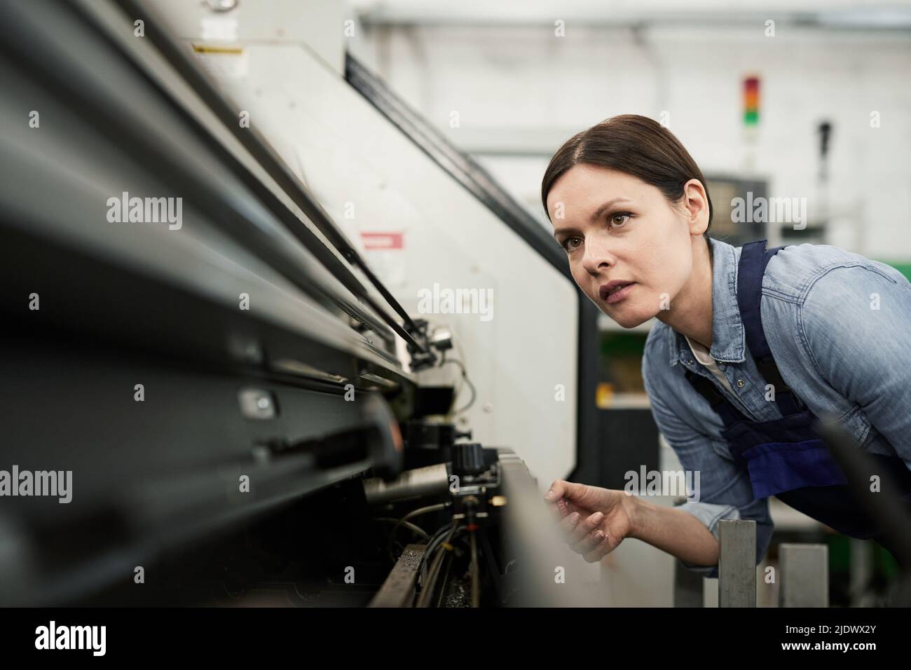 Content skilled brunette woman in workwear watching lathe machine ...