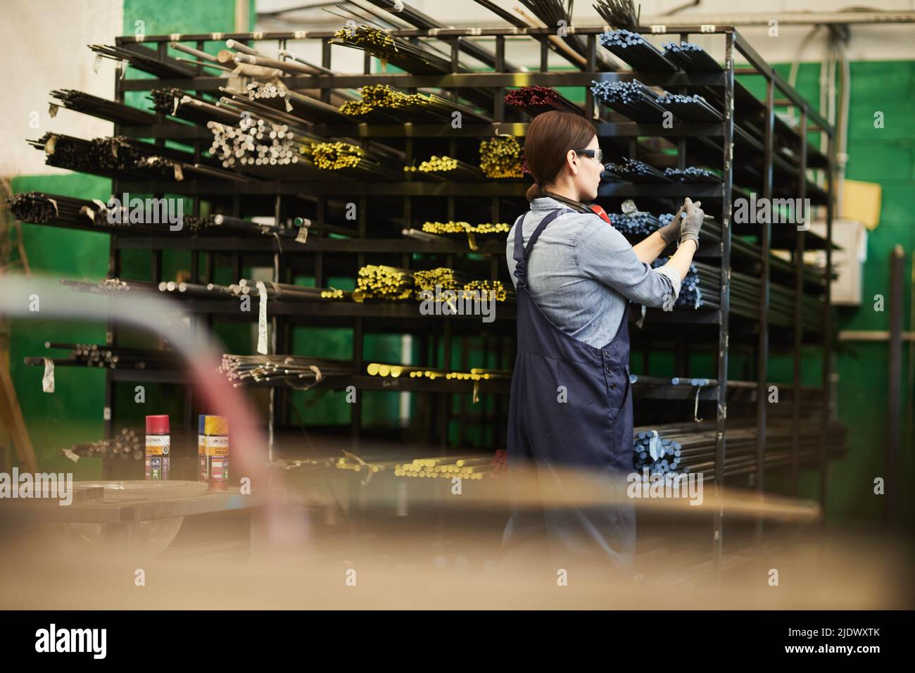 Rear view of female warehouse worker in overalls standing at metal ...