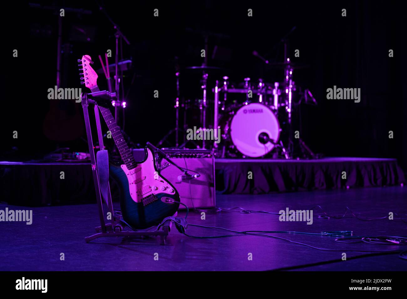 Electric guitar on stage with drum kit in the background under purple ...
