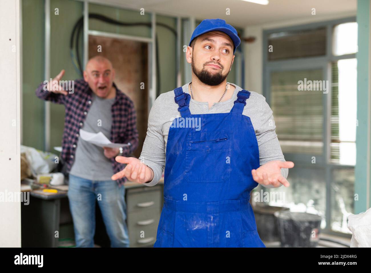 Perplexed builder in building under renovation with screaming customer ...