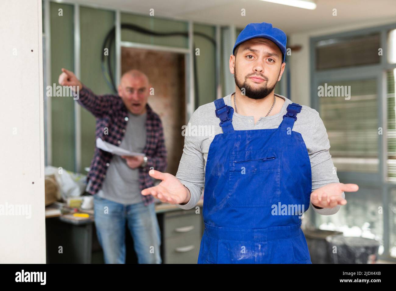 Perplexed builder in building under renovation with screaming customer ...