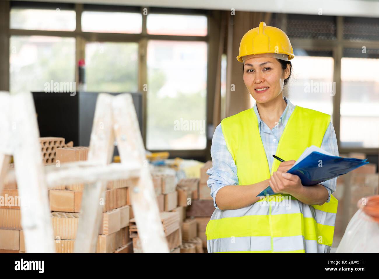 Woman foreman in a protective helmet and yellow vest checks the ...