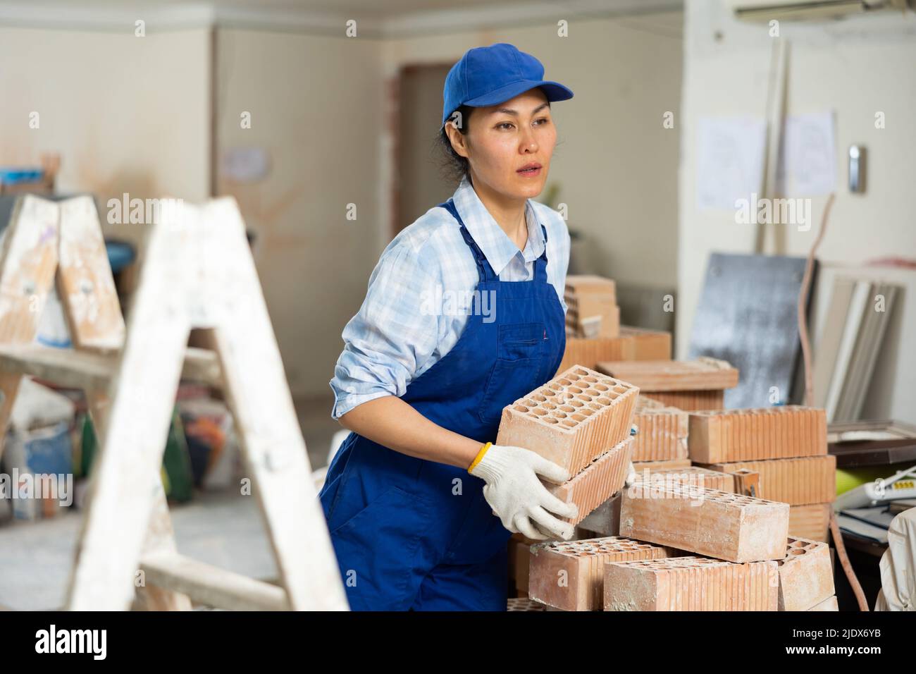 Female builder carrying bricks at renovating object Stock Photo - Alamy