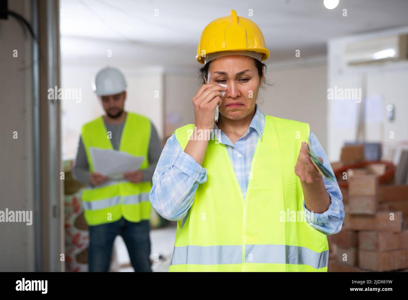 Crying construction workwoman standing at building site with banknotes ...