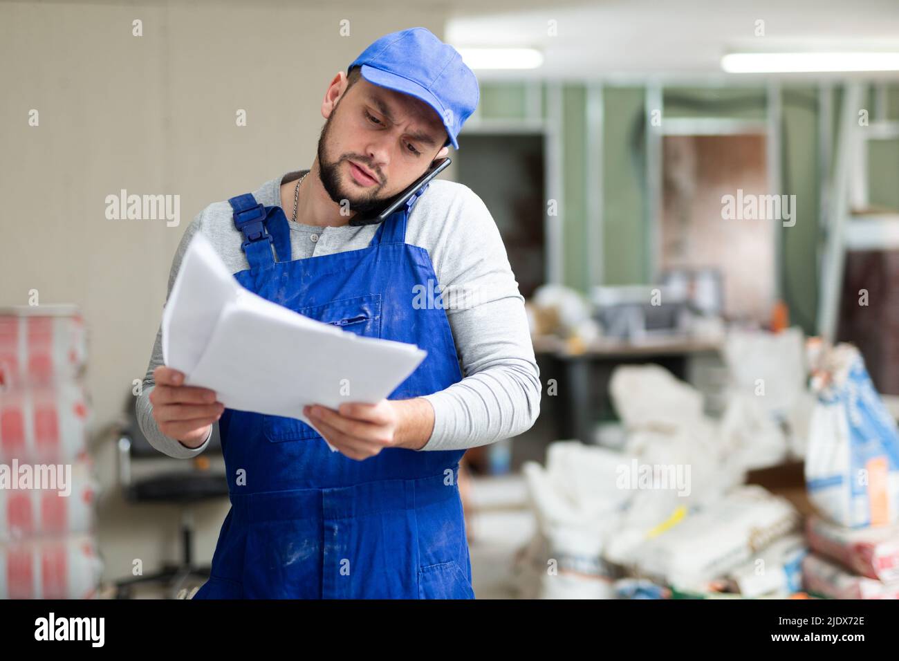 Master in blue overalls talking on mobile phone, discussing documents ...