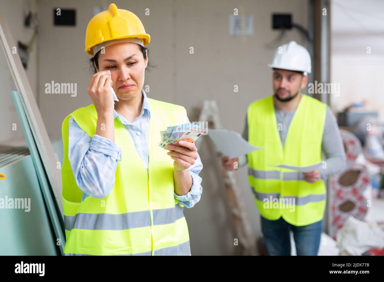 Crying female builder standing at construction site with banknotes in ...