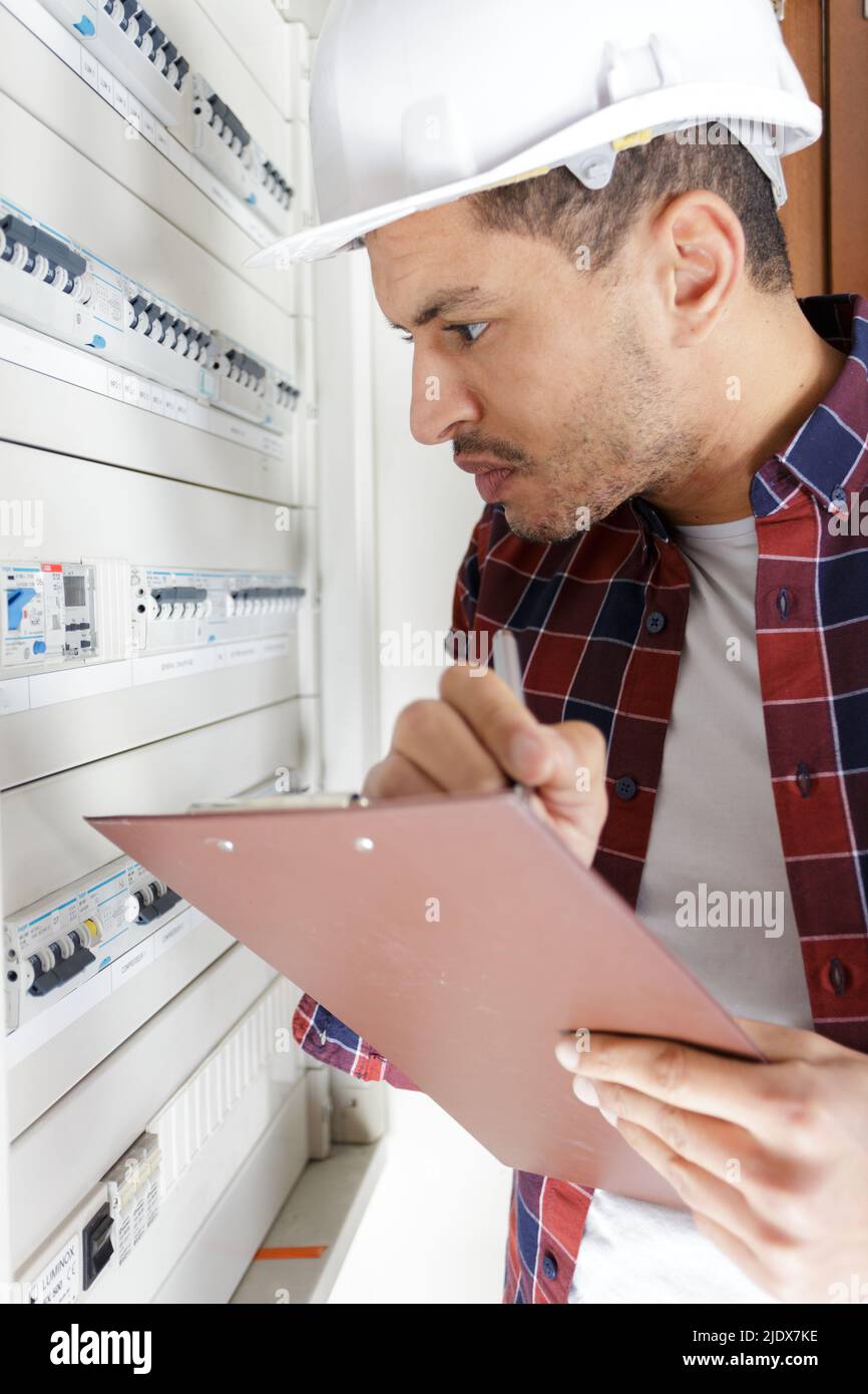 technician writing on clipboard in front of fuse box Stock Photo - Alamy