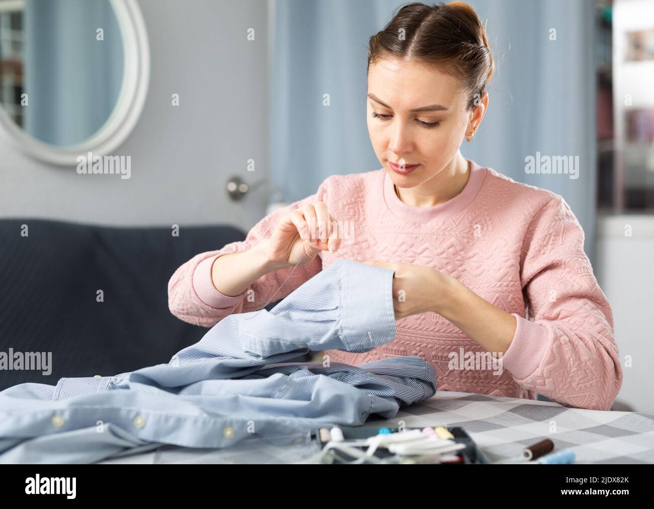 Woman repairing clothes with a needle and thread Stock Photo - Alamy